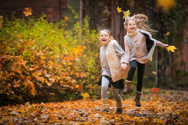 Dos niñas riendo corren juntas en un parque de otoño entre una hoja ... Dos niñas riendo corren juntas en un parque de otoño entre una hoja ...