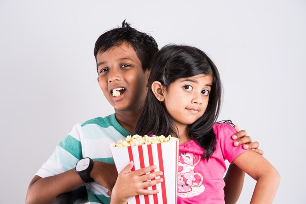 Lindo niño indio feliz y niña o hermanos comiendo palomitas de maíz y ... Lindo niño indio feliz y niña o hermanos comiendo palomitas de maíz y ...