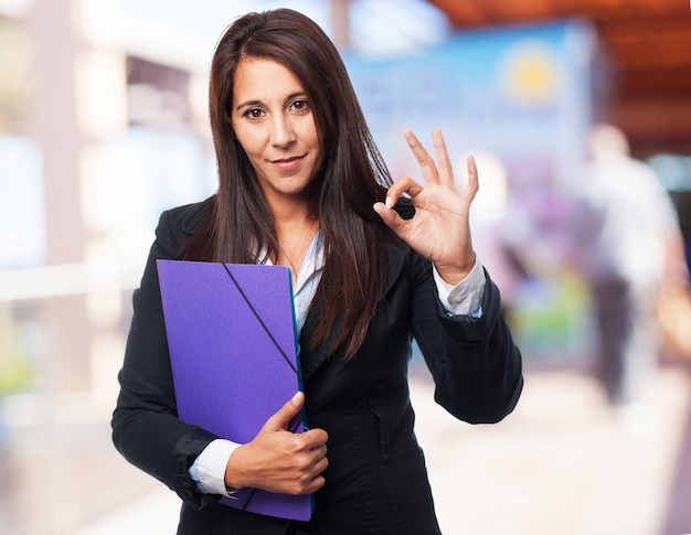 Mujer elegante haciendo ok con la mano y con una carpeta en la otra ... Mujer elegante haciendo ok con la mano y con una carpeta en la otra ...