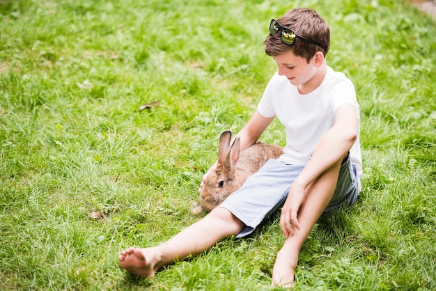 Niño pequeño sonriente que se sienta con el conejo en hierba verde ... Niño pequeño sonriente que se sienta con el conejo en hierba verde ...