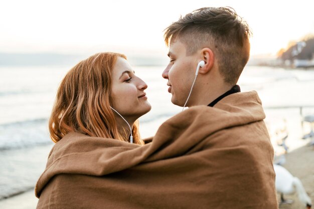 Pareja joven escuchando música con auriculares en la playa en invierno ... Pareja joven escuchando música con auriculares en la playa en invierno ...