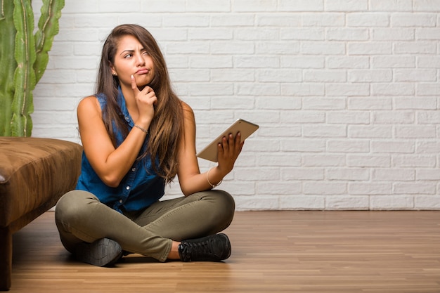 Retrato de la mujer latina joven que se sienta en el piso que piensa y ... Retrato de la mujer latina joven que se sienta en el piso que piensa y ...