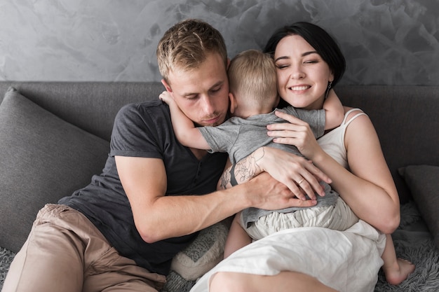 Vista posterior de un niño pequeño abrazando a sus padres sentados en ... Vista posterior de un niño pequeño abrazando a sus padres sentados en ...