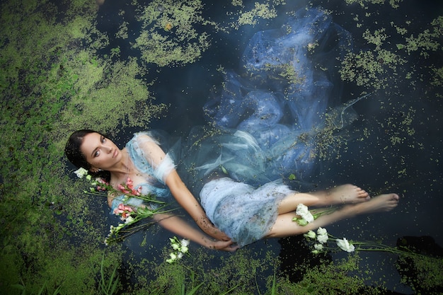 Premium Photo Art Beautiful Romantic Woman Lies In Swamp In Blue Long Dress With Flowers
