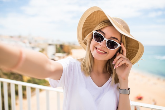 Free Photo Cheerful Young Woman In Hat And Sunglasses Taking Selfie With Mobile Phone On