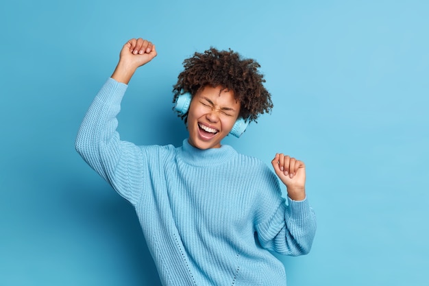 Free Photo Joyful Dark Skinned Curly Woman Dances Carefree Raises Arms Feels Optimistic Wears