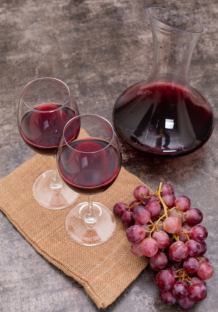 Free Photo Side View Red Wine In Jug And Glasses On Sackcloth On Dark Stone Vertical