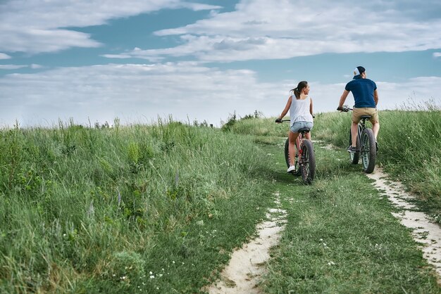 Premium Photo Young Happy Couple Ride Bicycles In The Meadow Back To