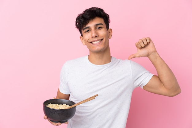 Young Man Holding A Bowl Of Noodles Over Isolated Wall Premium Photo