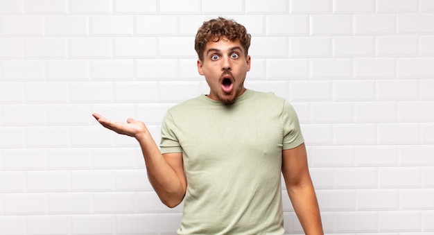 Jonge man die verrast en geschokt kijkt, met open mond terwijl hij een ... Jonge man die verrast en geschokt kijkt, met open mond terwijl hij een ...